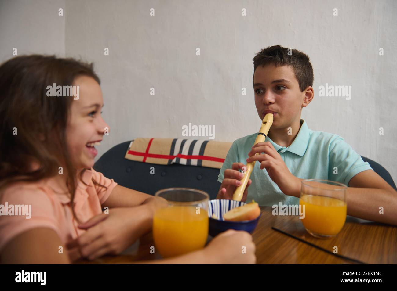 A boy plays a flute while a cheerful girl listens amusedly. They sit ...
