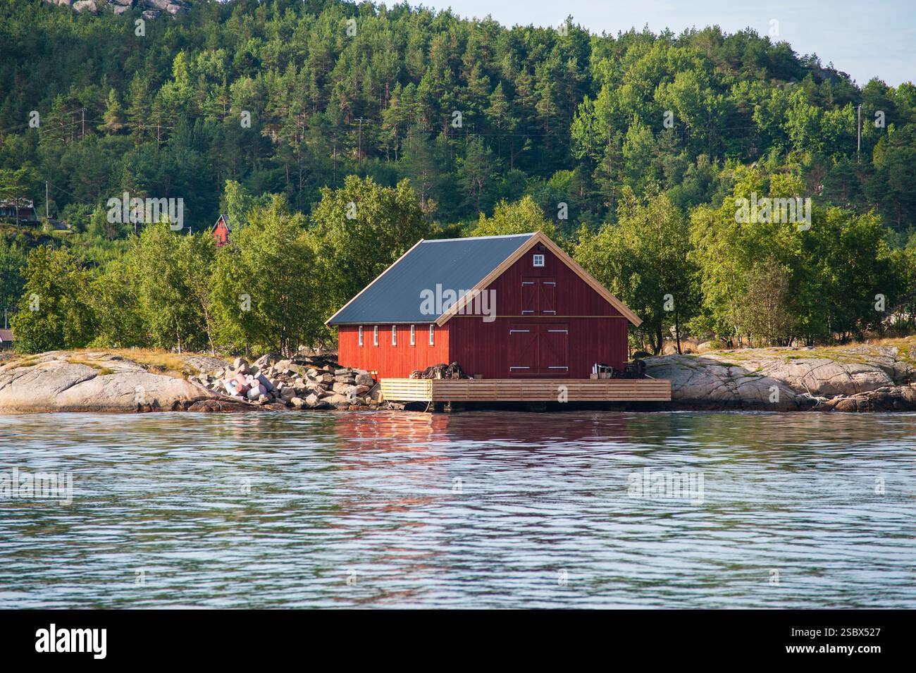red wooden boathouse on rocky shoreline with forest backdrop Stock ...