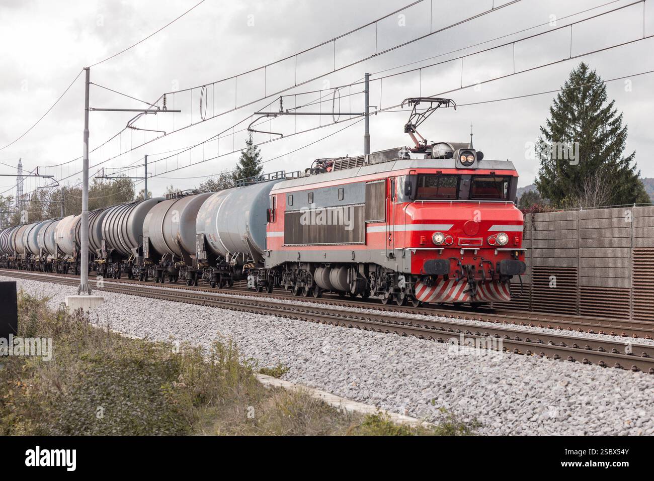 Red electric locomotive is hauling a freight train consisting of tank ...