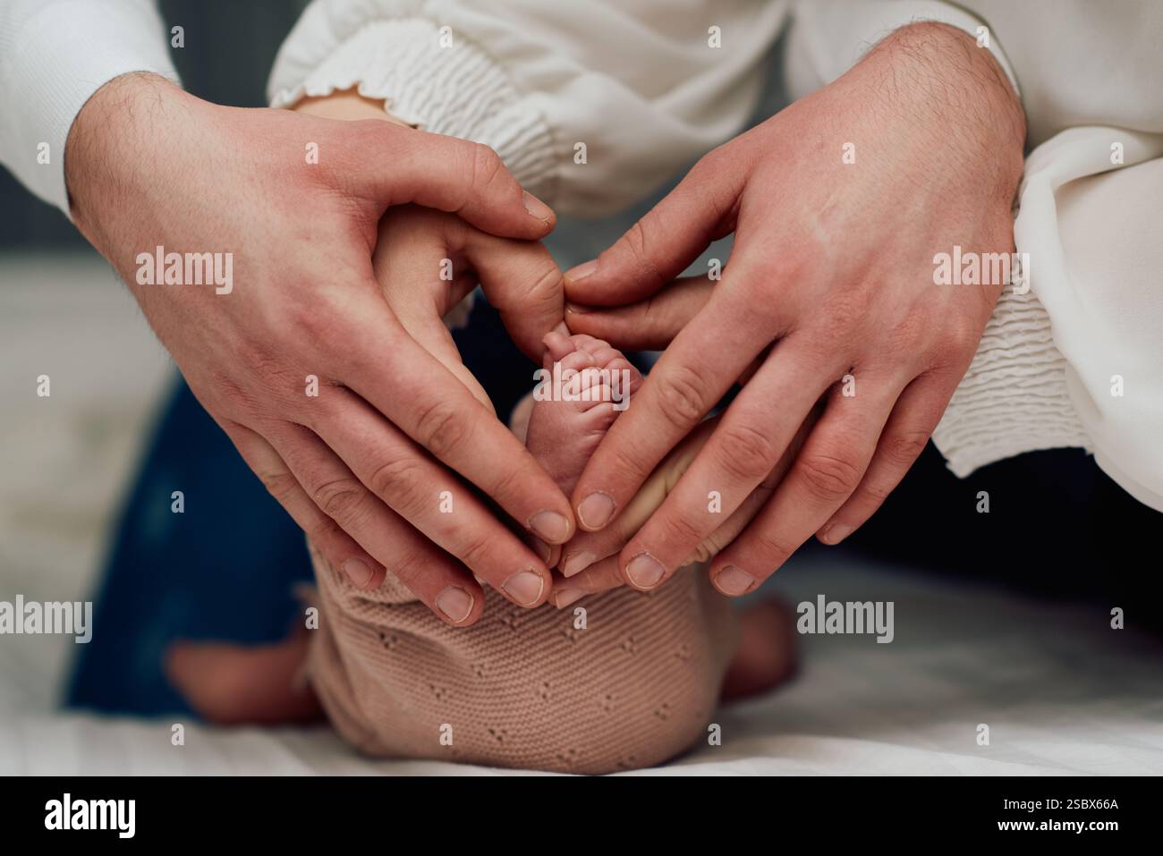 A close up of parents hands forming a heart around their newborns tiny ...