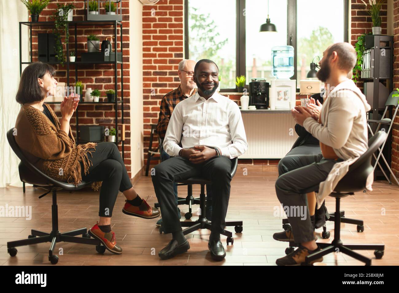 Smiling black guy sitting in middle of room as fellow members ...
