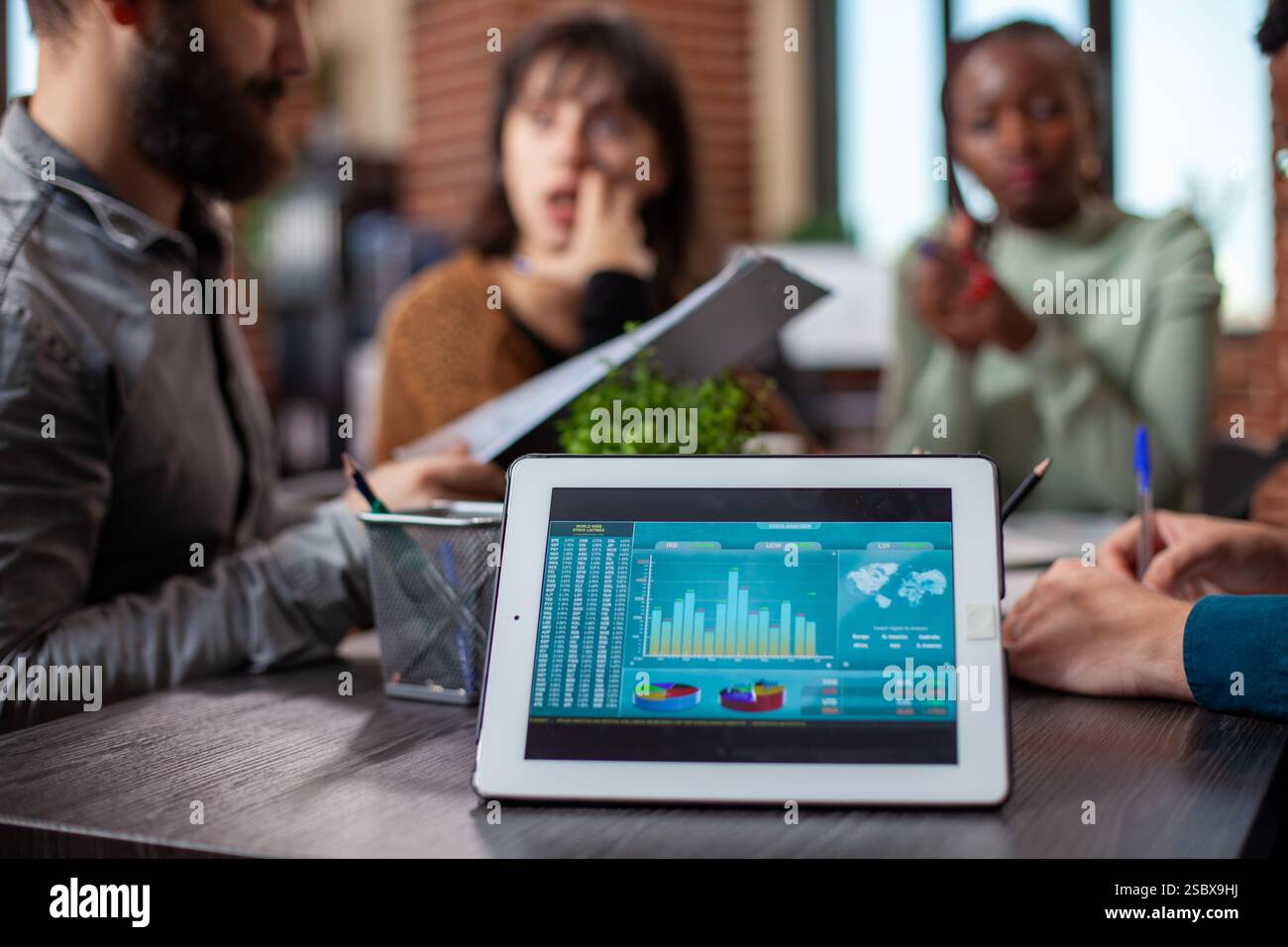 Closeup of tablet showing financial graphs as coworkers discuss ...