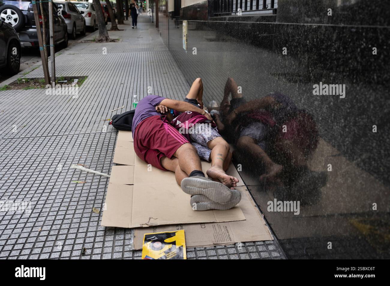 A couple sleeps atop pieces of cardboard outside a residential building ...