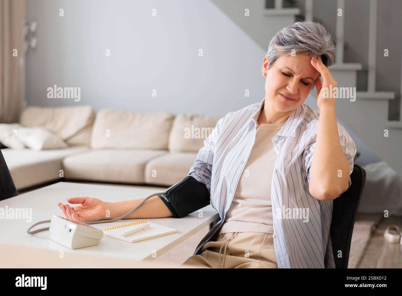A beautiful woman in age with gray hair measures blood pressure with ...