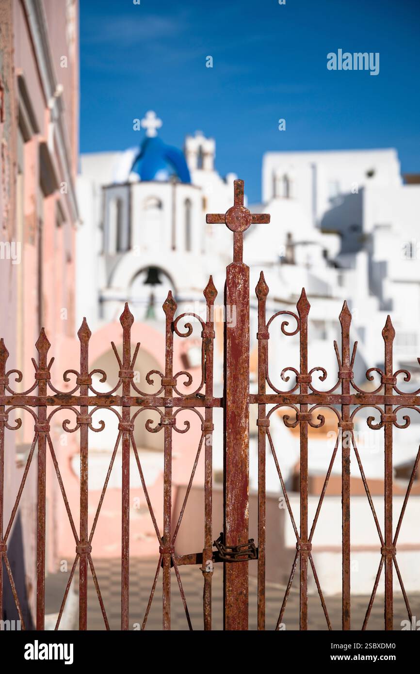 Rusty wrought-iron entrance gate in front of white houses and a church ...