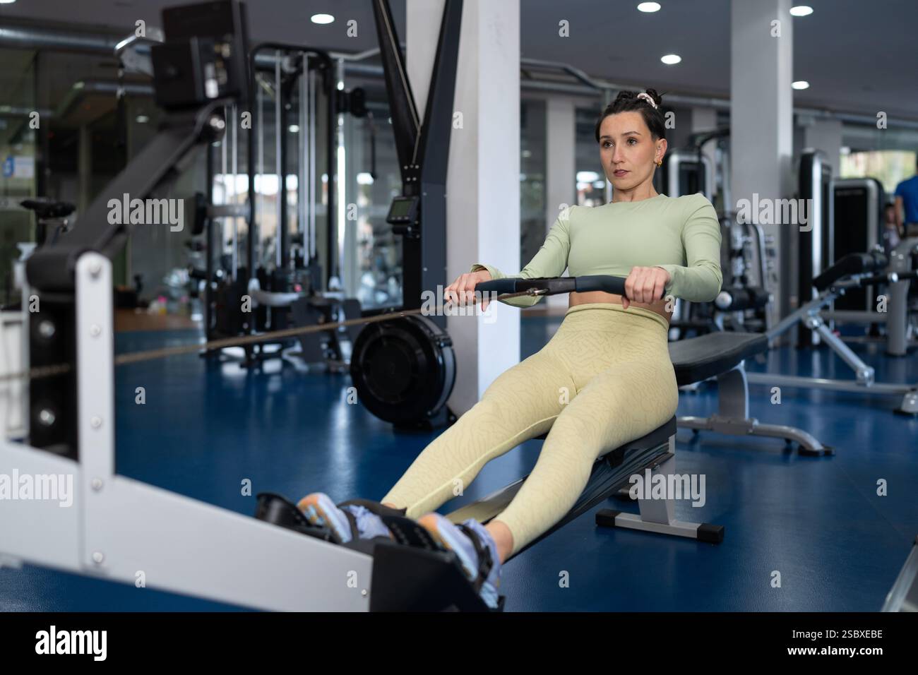 Focused female athlete performing rowing exercise on a fitness machine ...