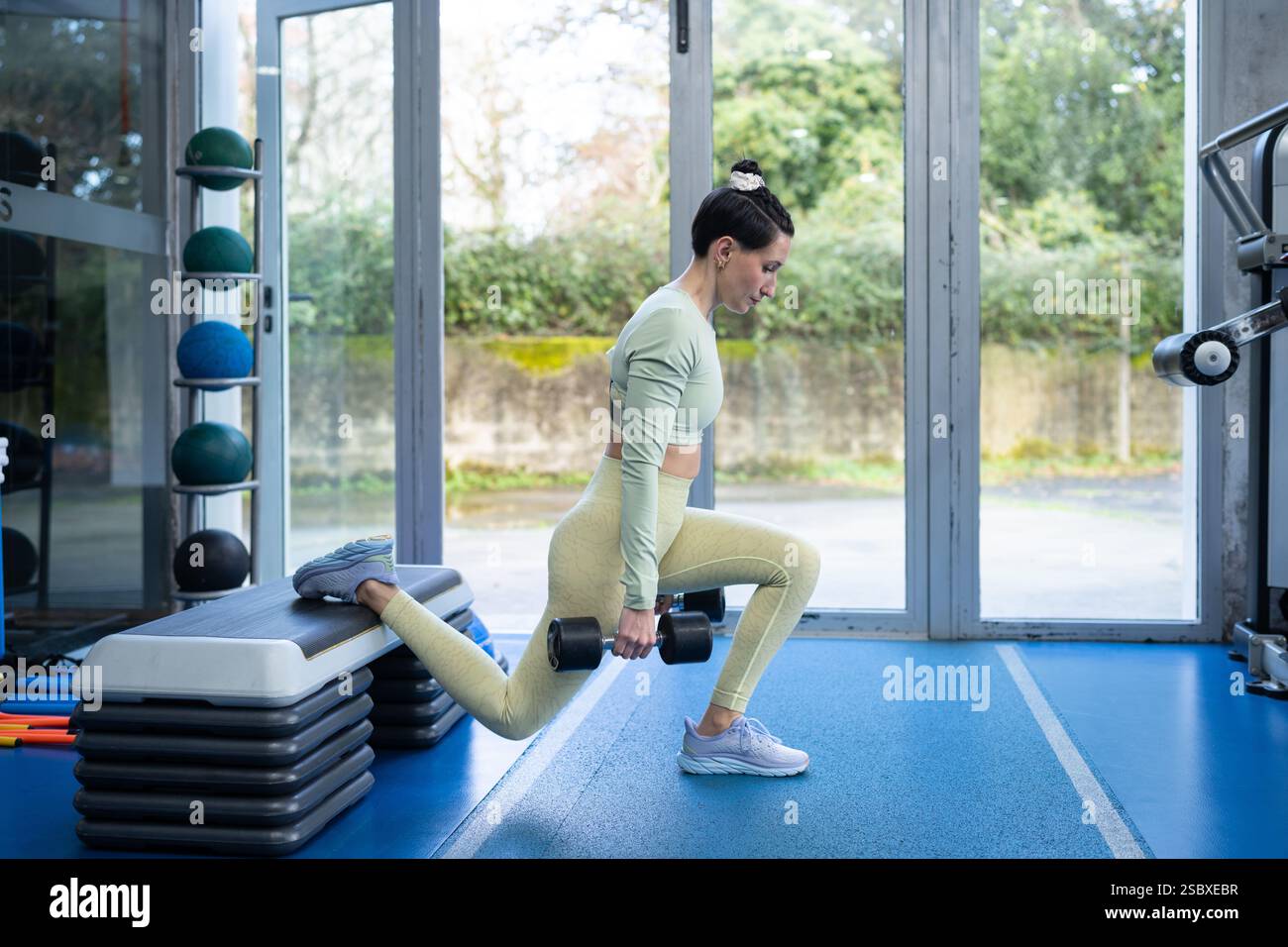Young athletic woman is doing bulgarian split squats with dumbbells in ...