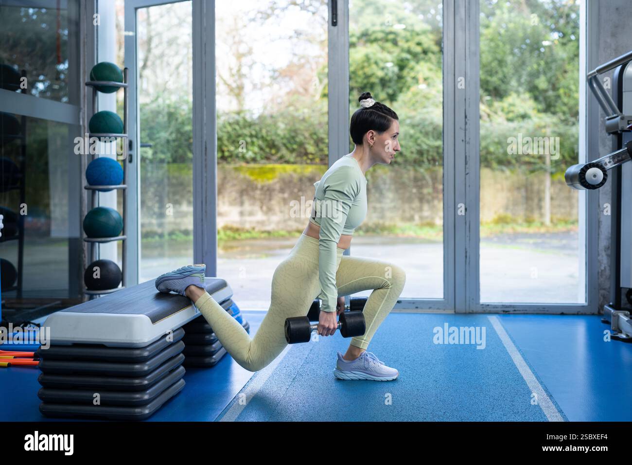 Female athlete performing bulgarian split squat exercises with dumbbells on a stepper in a ...