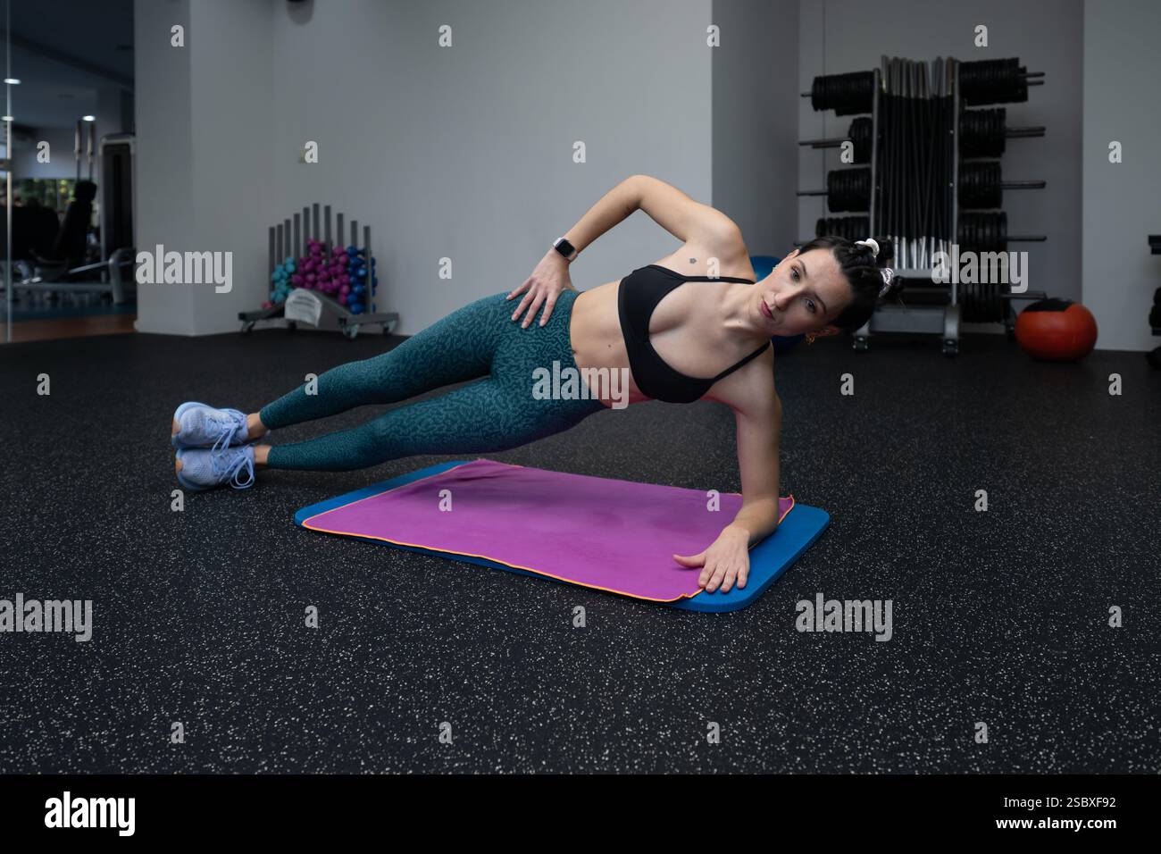 Female athlete performing side plank exercise on fitness mat, engaging core muscles and ...