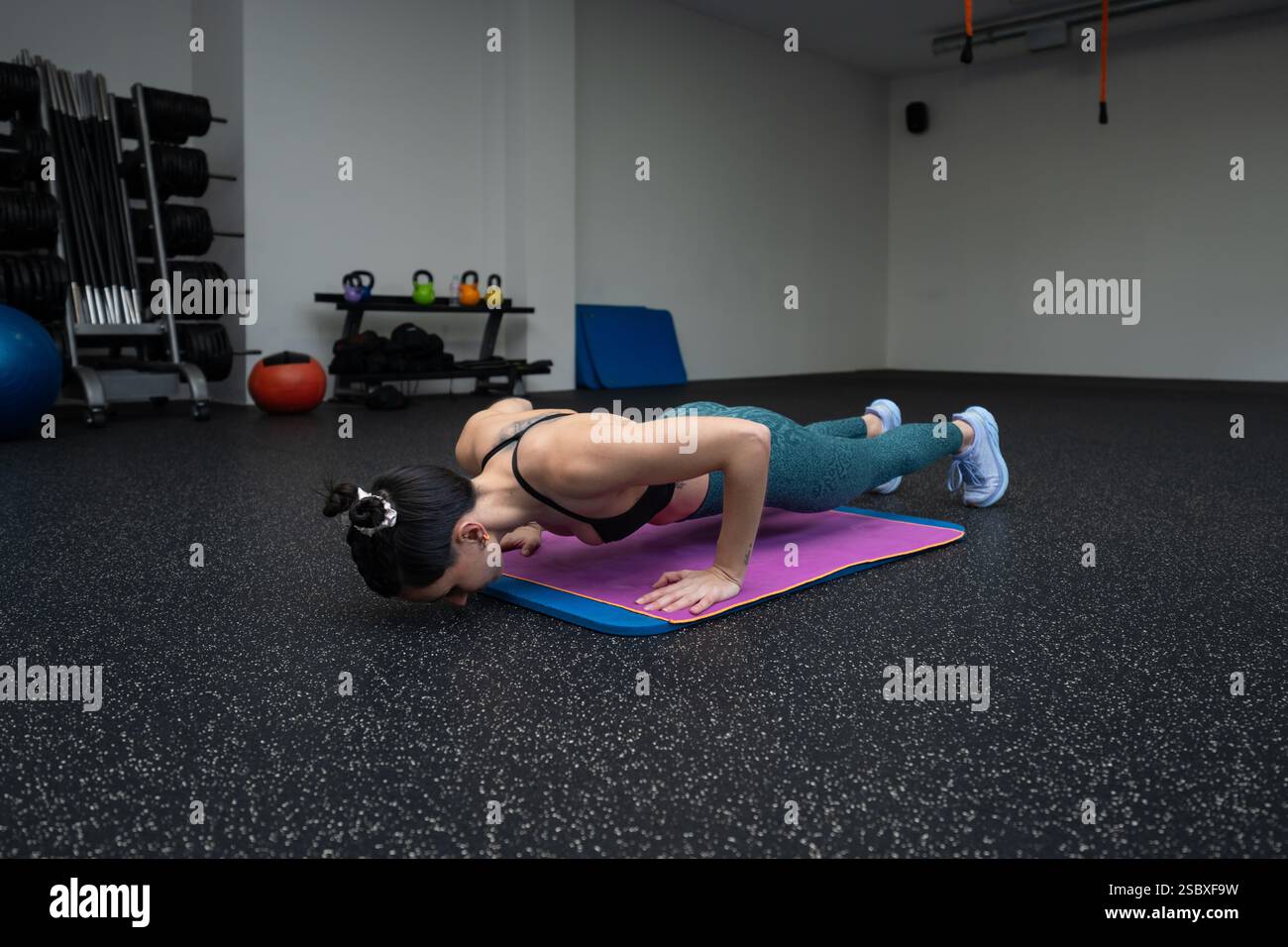Young athletic woman performing push ups on a mat in a gym ...