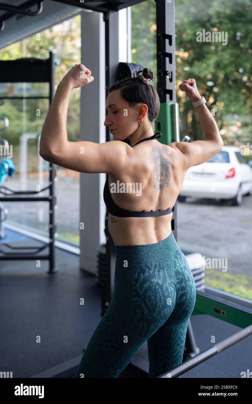 Strong woman flexing her biceps in a gym, demonstrating impressive fitness levels and unwavering ...