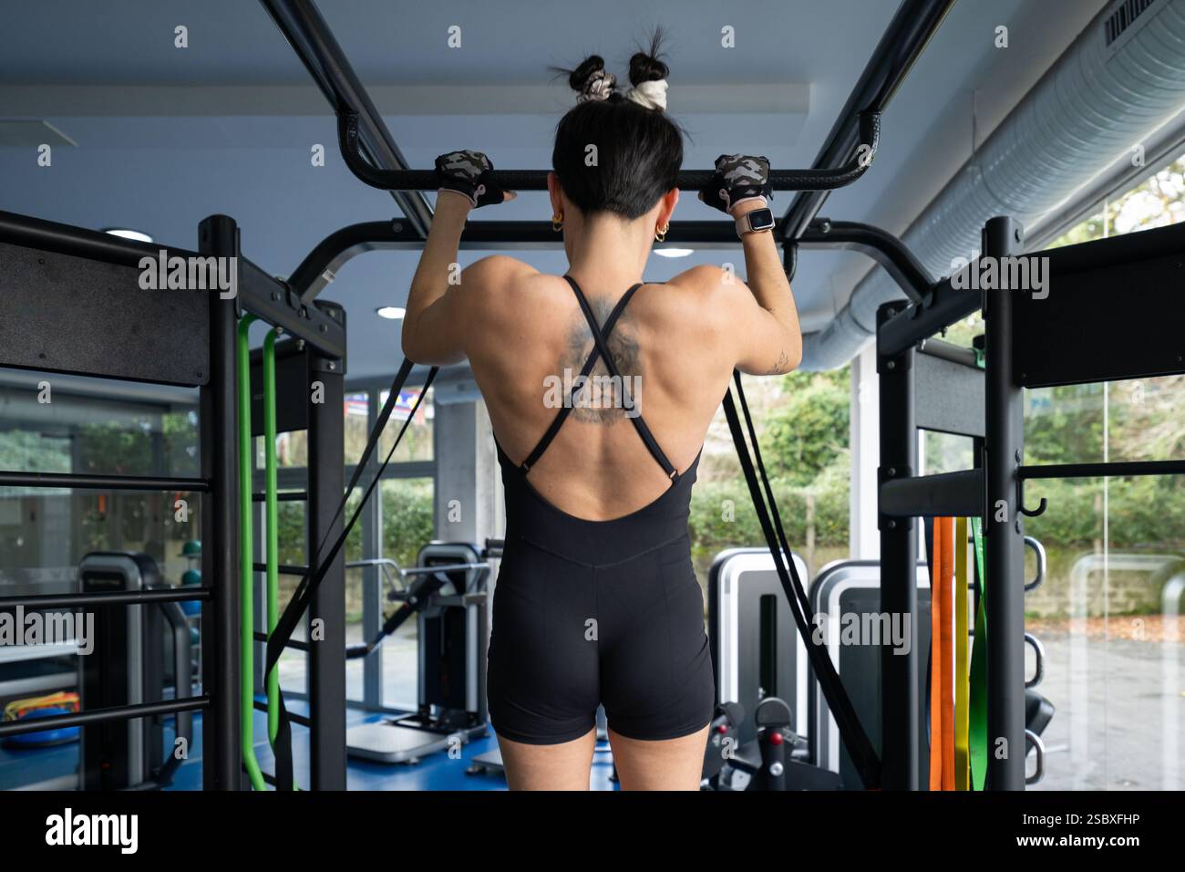 Muscular female executing pull ups in sleek black bodysuit, revealing defined back muscles ...
