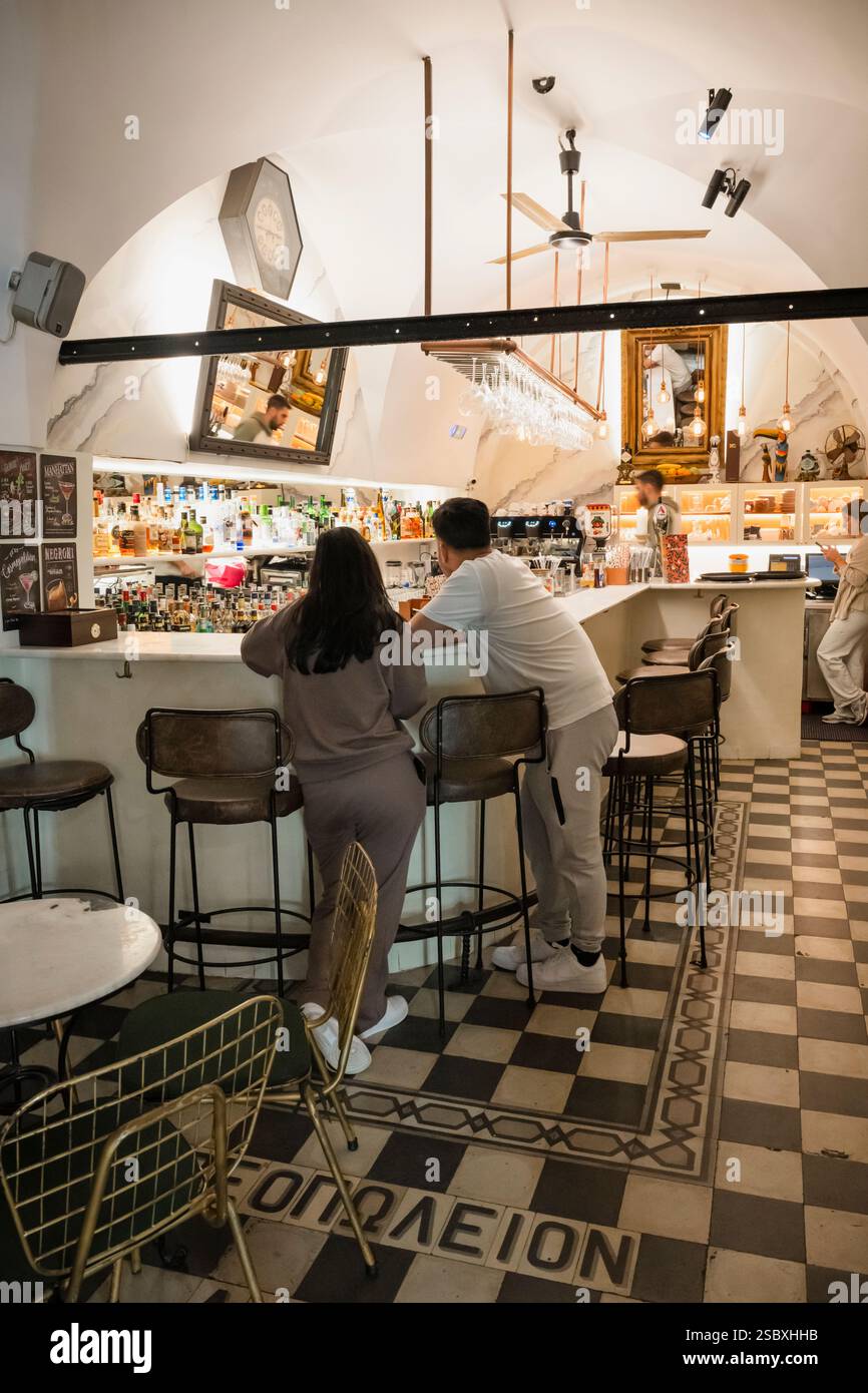 A young couple at the counter of the Hassapiko Bar in Oia, Santorini ...