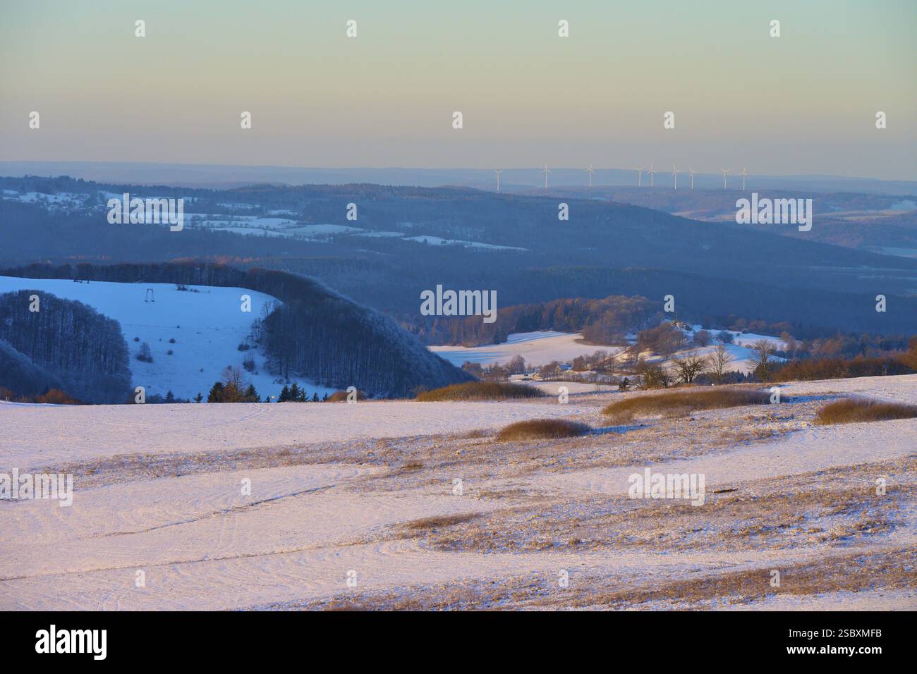 Hilly snowy landscape with wind turbines on the horizon under a blue ...