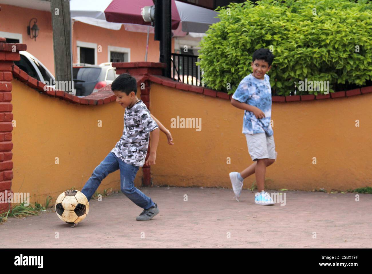 Two 9-year-old poor dark-skinned Latino boys play soccer in the street ...