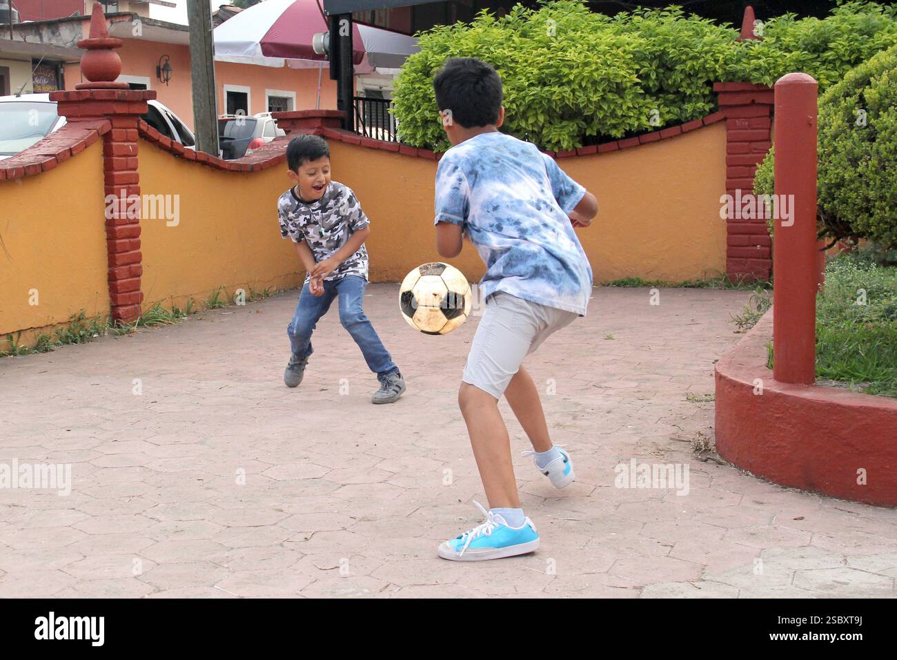 Two 9-year-old poor dark-skinned Latino boys play soccer in the street ...