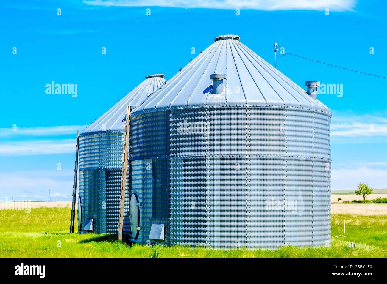 Two large metal silos are sitting in a field. The silos are empty. The ...