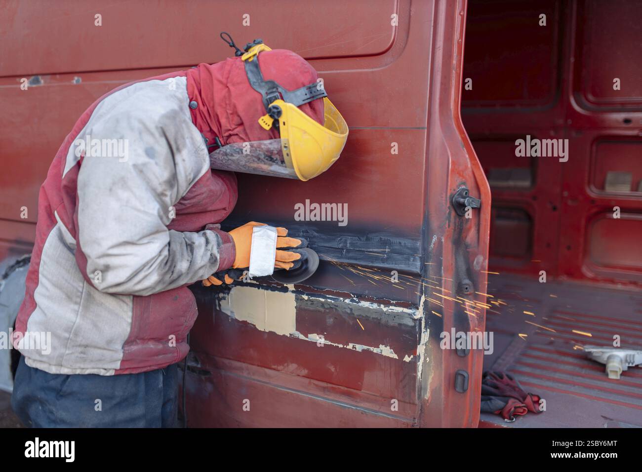 Sanding the body of a van, a worker produces sparks during the process ...