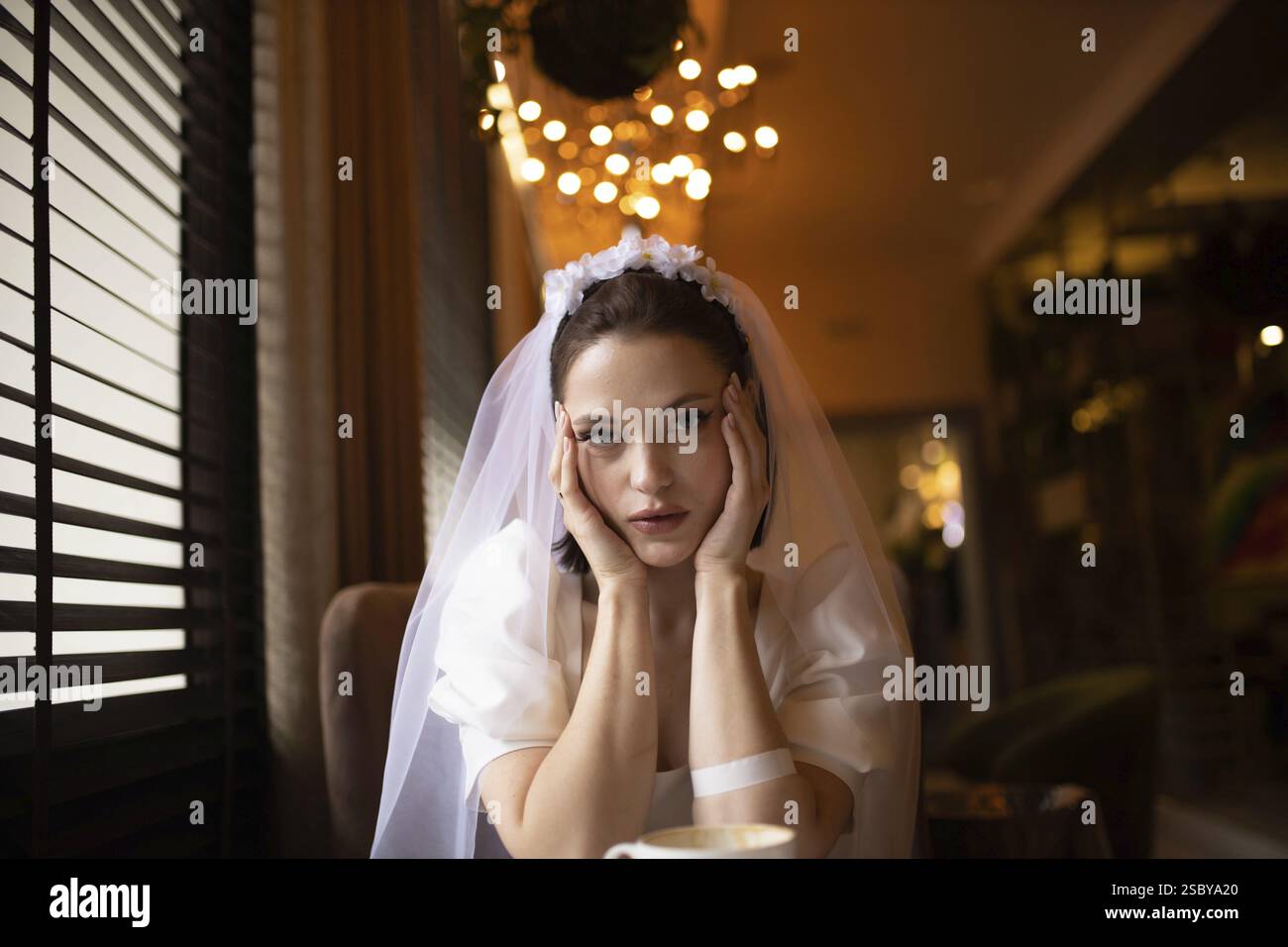 Bride in contemplative mood with hands on face in softly lit cafe Stock ...