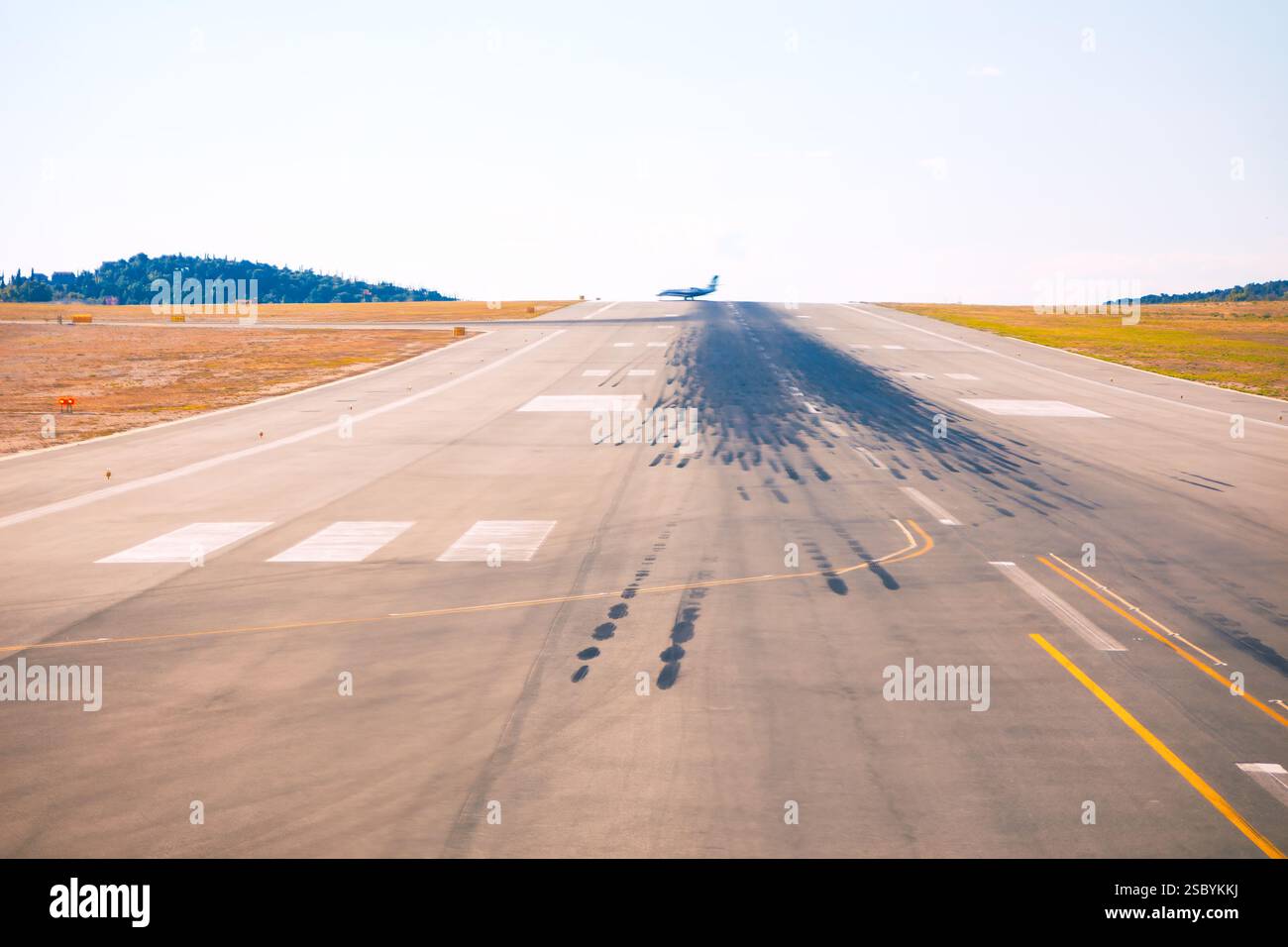 Long airport runway with tire skid marks leading to departing airplane ...