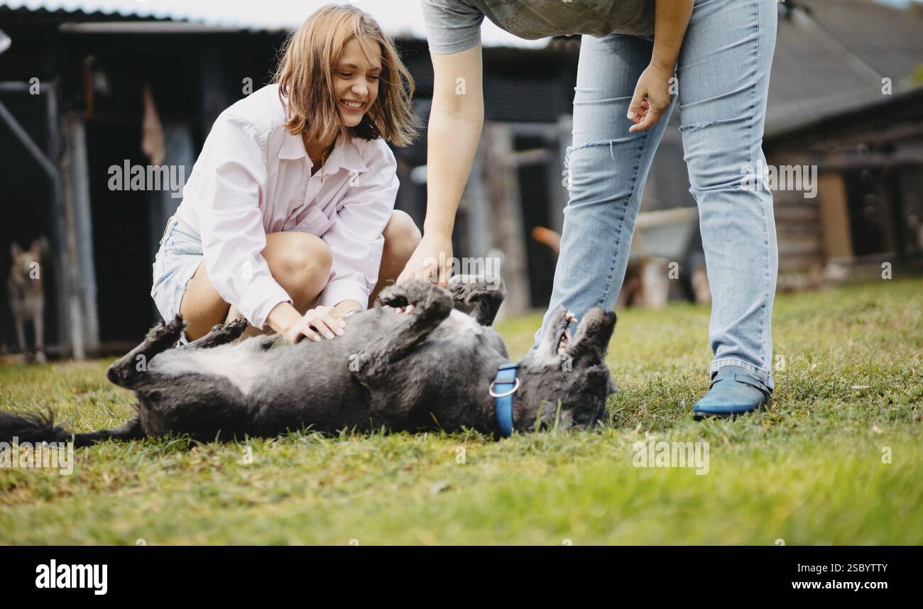 Two women enjoying playful interaction with a dog in a grassy area ...
