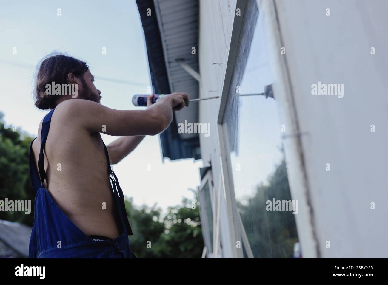 A man applying sealant to a window frame of a wooden structure during renovation Stock Photo - Alamy