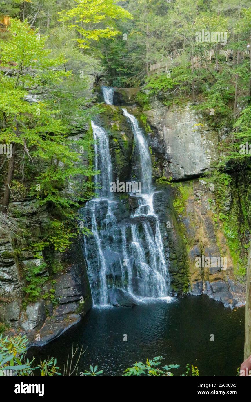 Water cascades down a rocky cliff into a tranquil pool, with visitors ...