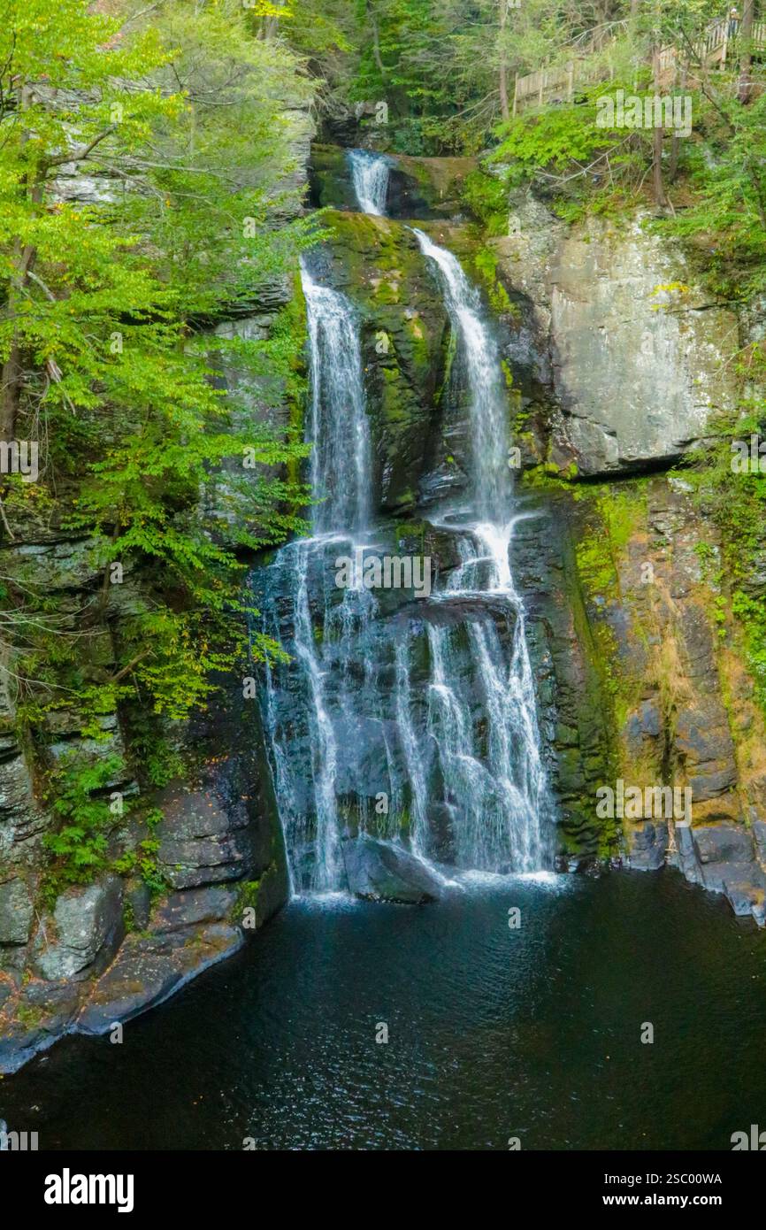 Water cascades down a rocky cliff into a tranquil pool, with visitors ...
