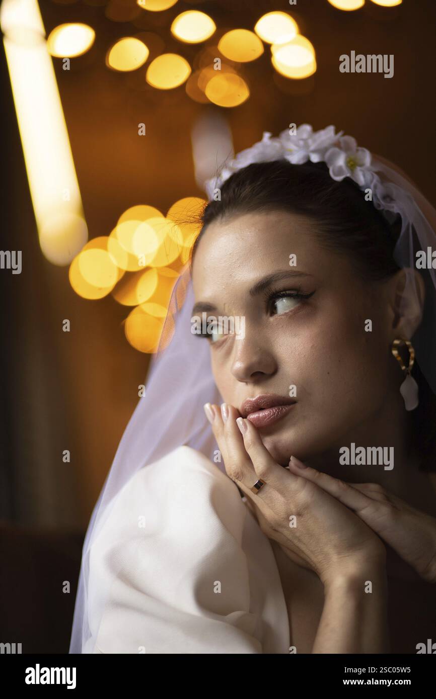 Bride with thoughtful expression, hands on chin, golden bokeh in ...