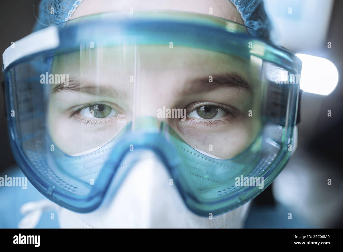 Doctor with surgical goggles and mask in a blue-toned environment ...