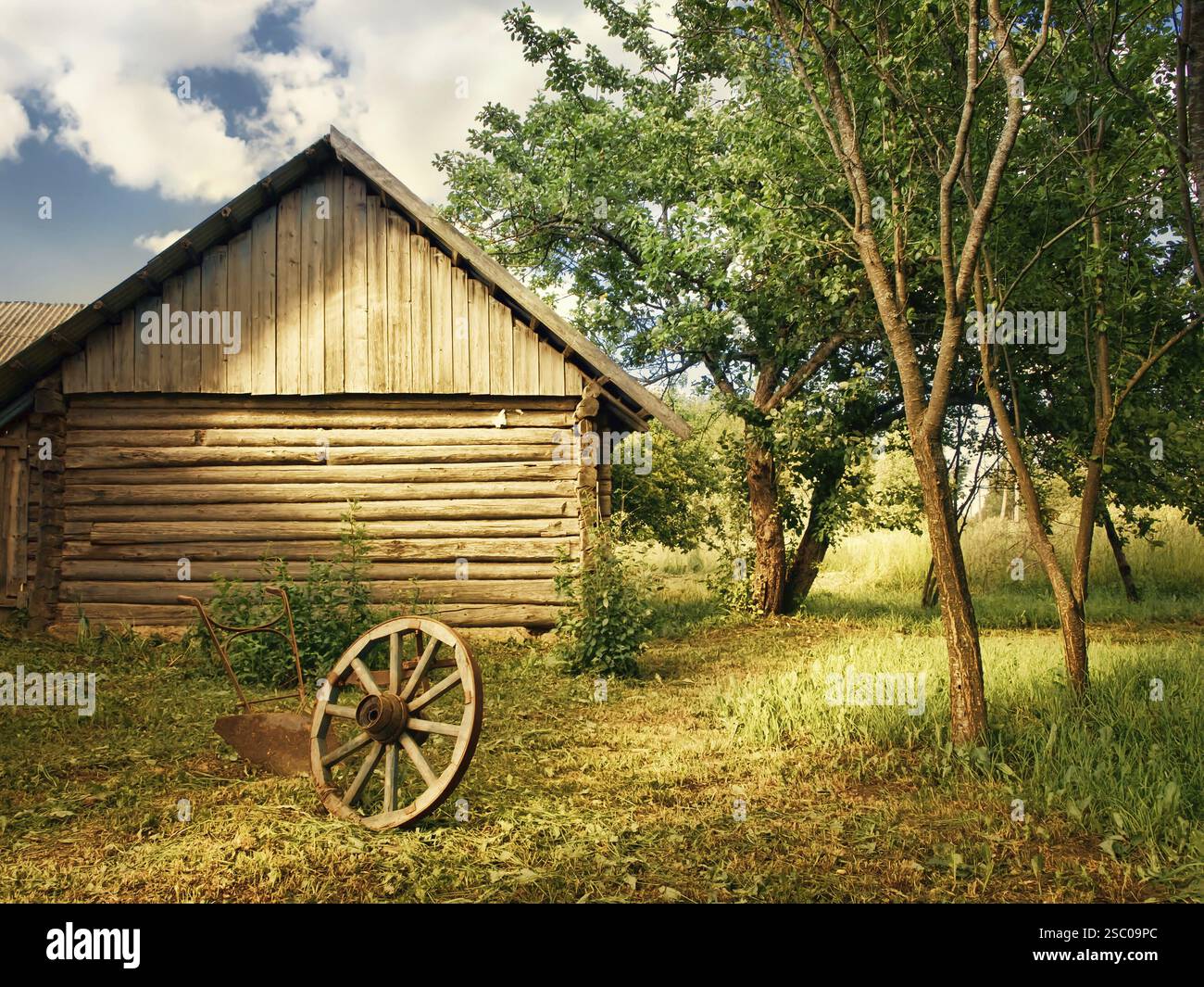 Country yard with trees, wheel and plough Stock Photo - Alamy