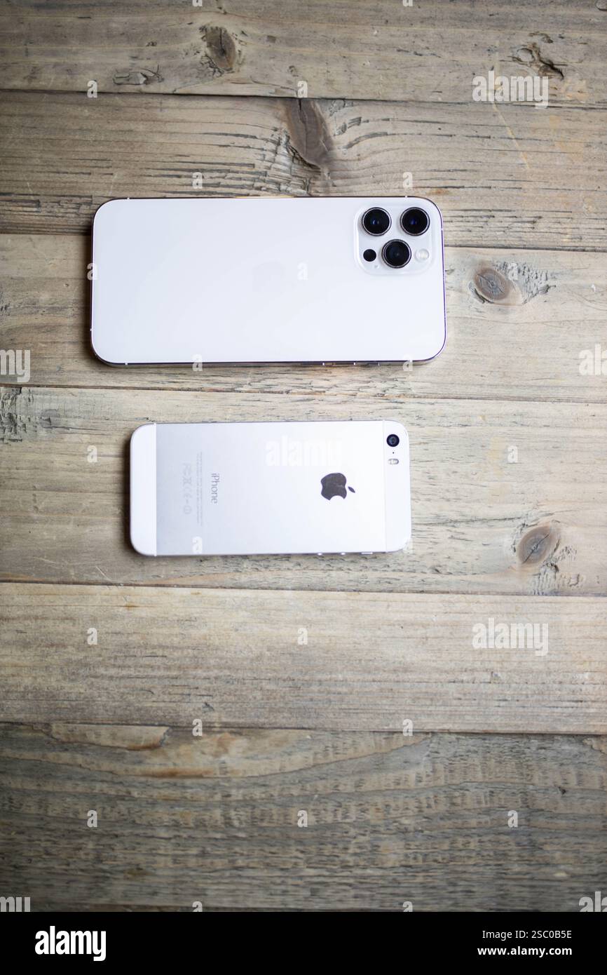 Two iPhones, one modern and one older model, placed on a wooden surface ...