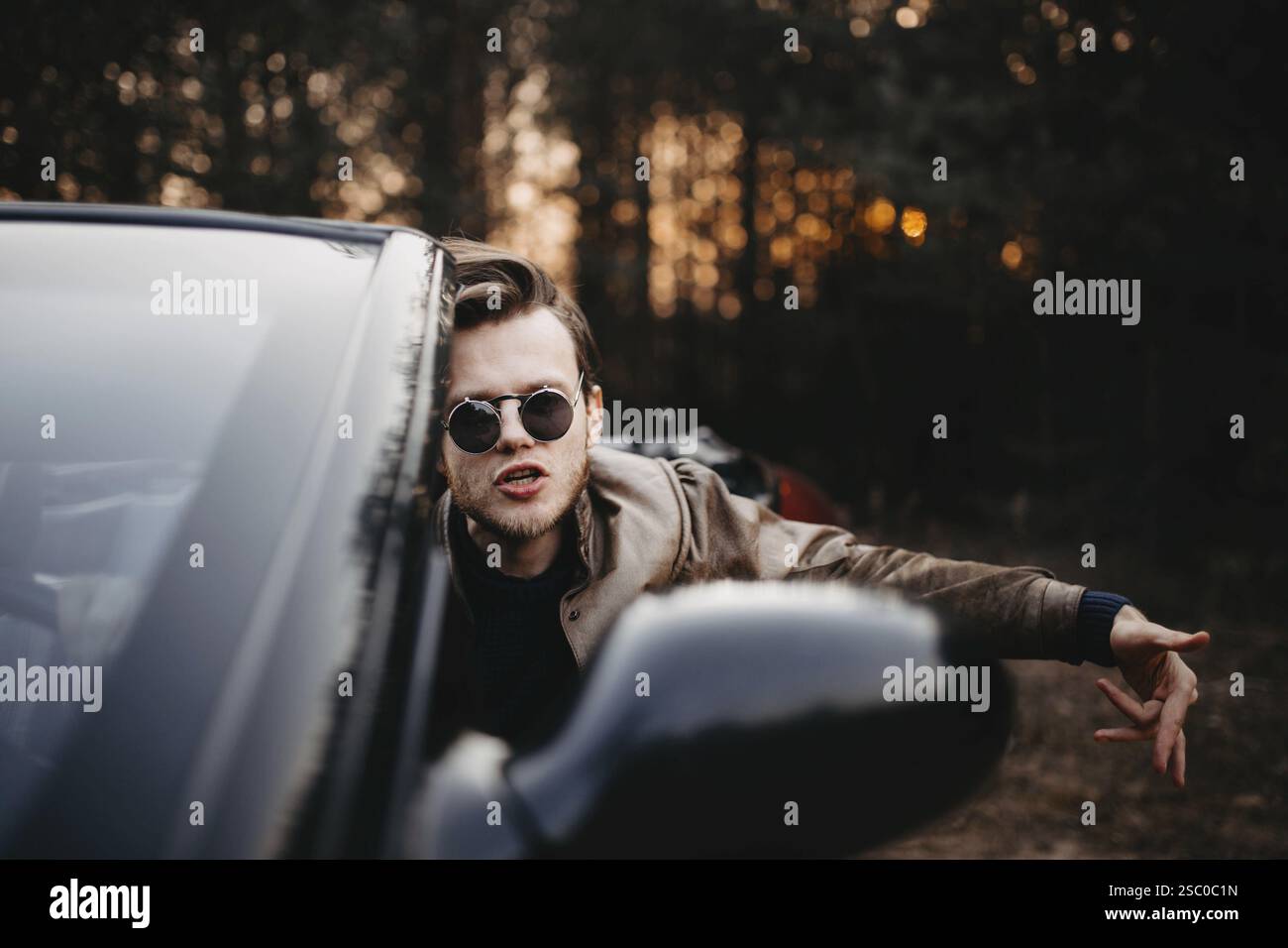 Man leaning out of a car window, wearing sunglasses, in a sunset ...