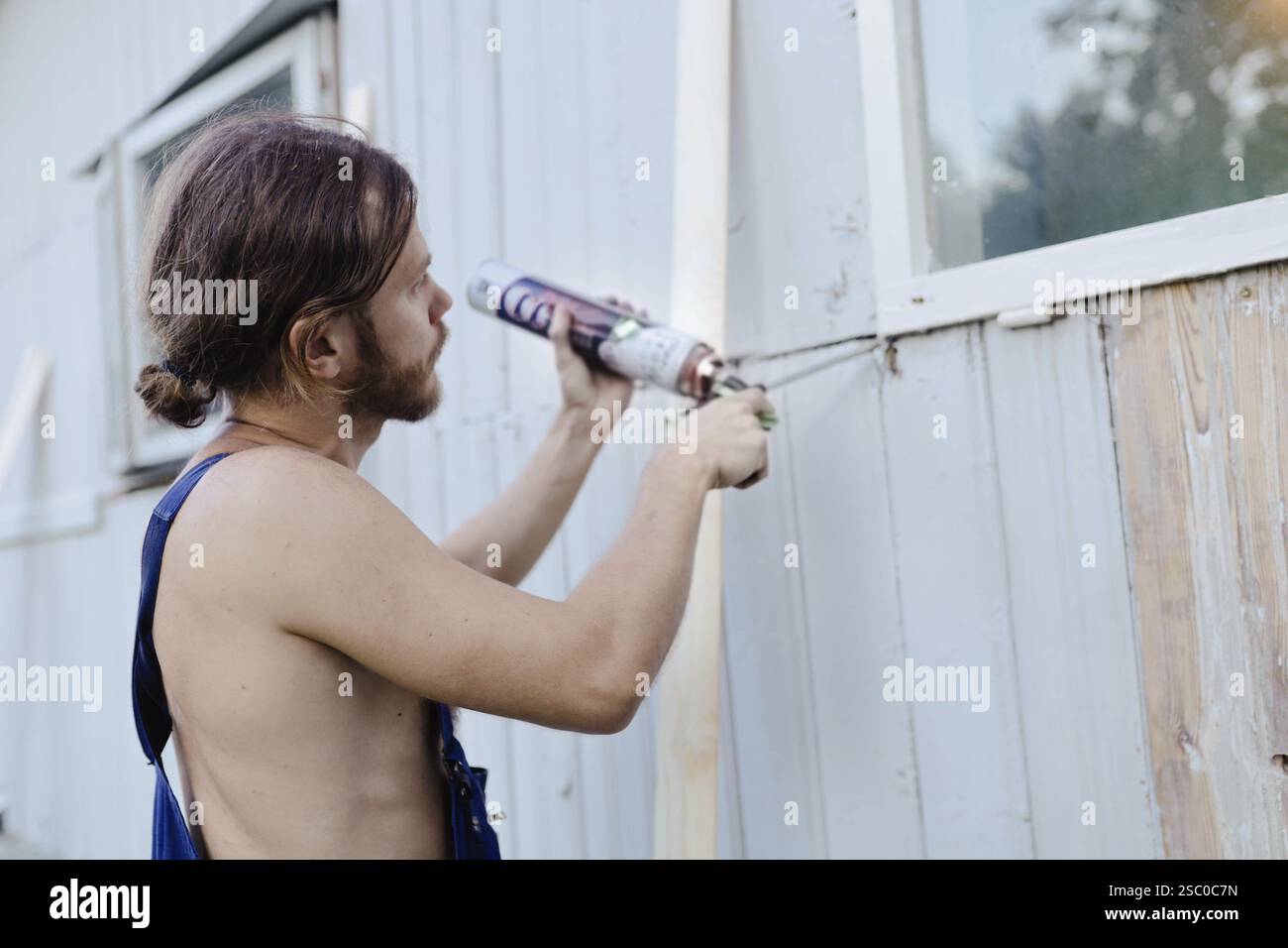 A man applying sealant around a window frame during an outdoor renovation Stock Photo - Alamy