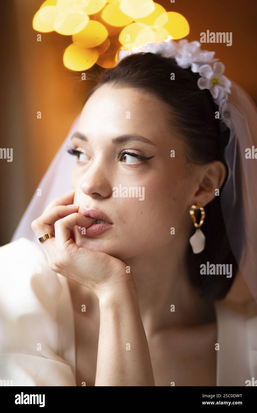 Bride with a veil, hand on chin, in soft lighting, conveying a ...
