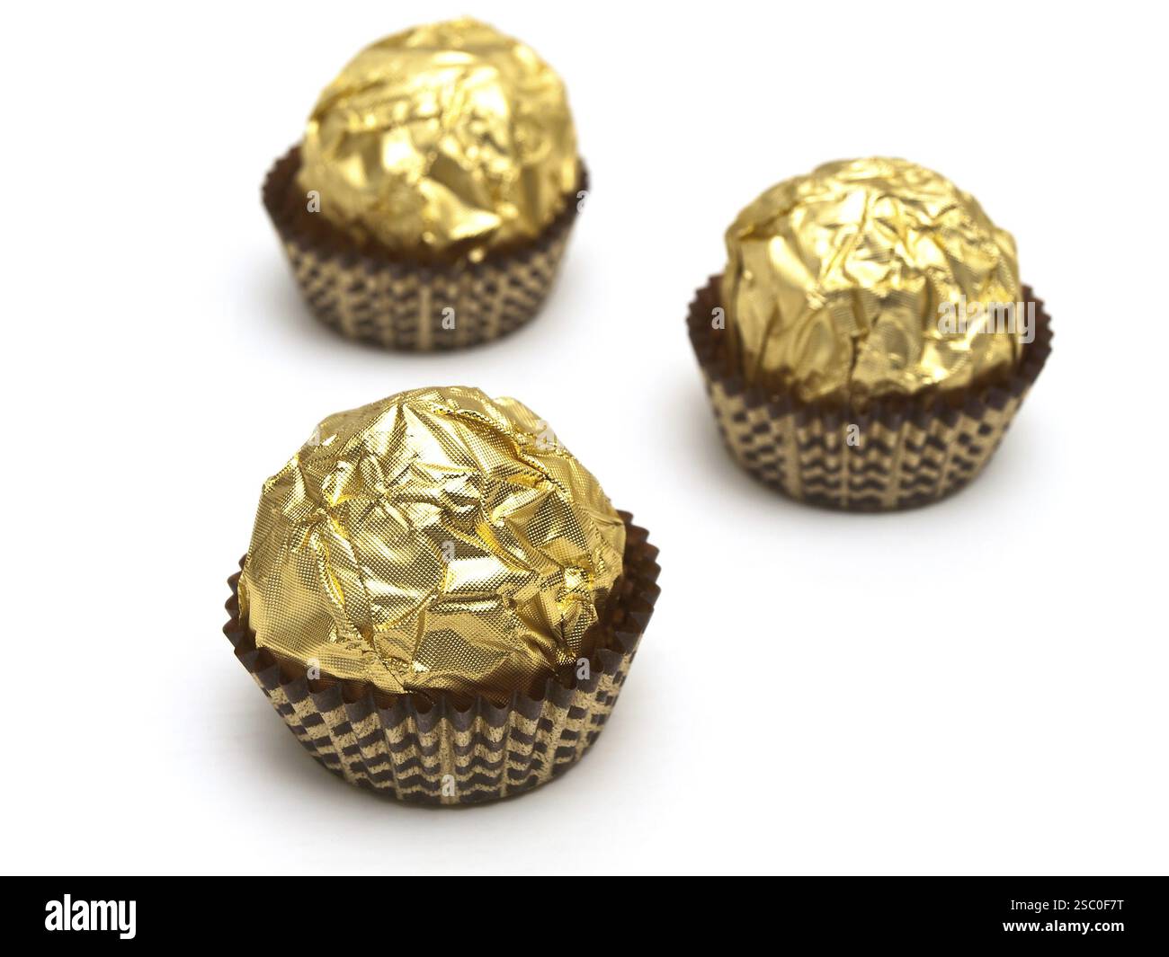 Three candies in gold paper over the white background Stock Photo - Alamy