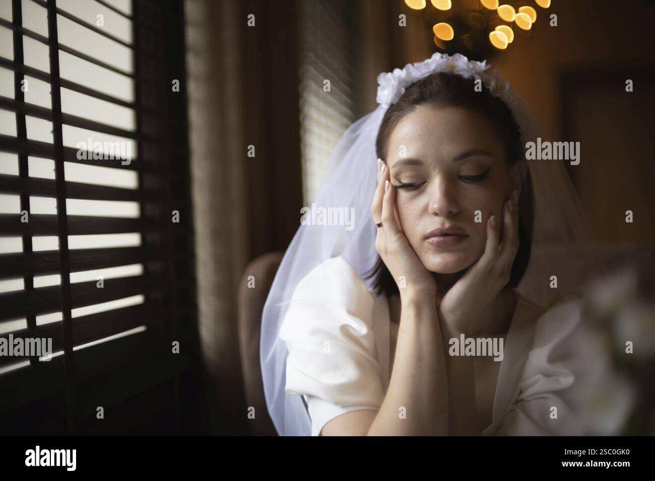 Bride with contemplative expression, sitting by the window with bokeh ...