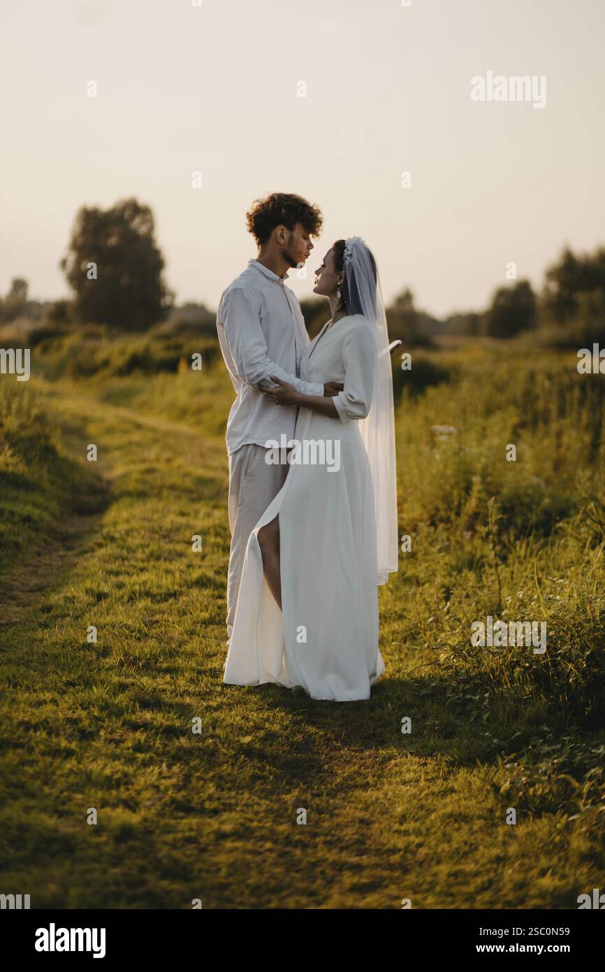 A couple shares an intimate moment on a grassy path during sunset ...