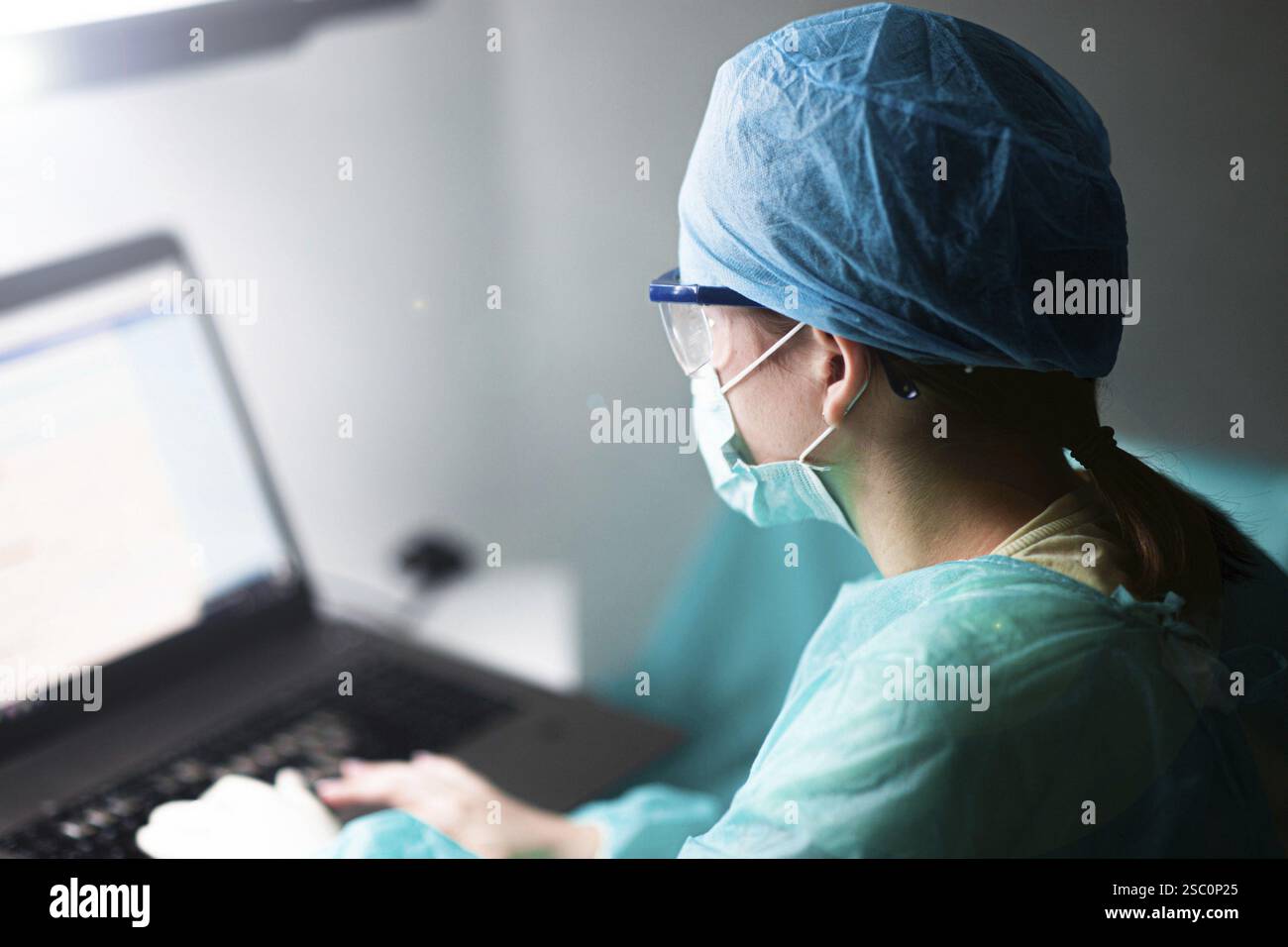 A healthcare worker in blue scrubs working on a computer at a desk ...