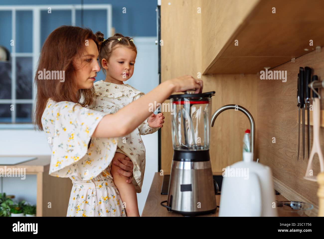 Mother use blender to prepare food with small child in her arms Stock ...
