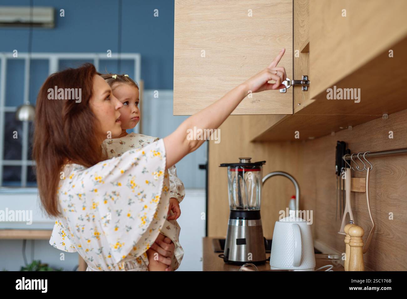 Woman opens kitchen cupboard, takes out food to cook with baby, kitchen ...