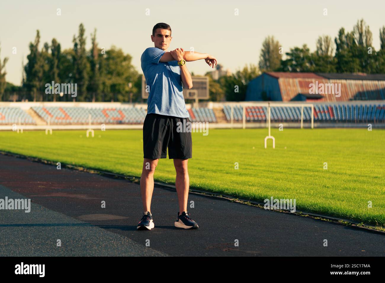 Young athlete stretches on a track field during golden hour in a ...