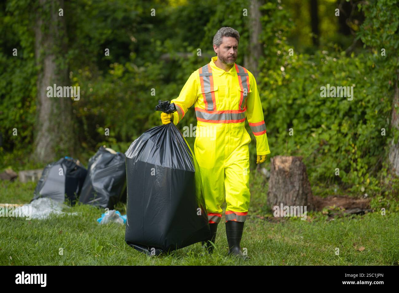 Volunteer in rubber gloves with trash bag clean up garbage on forest outdoor. Eco, environment ...