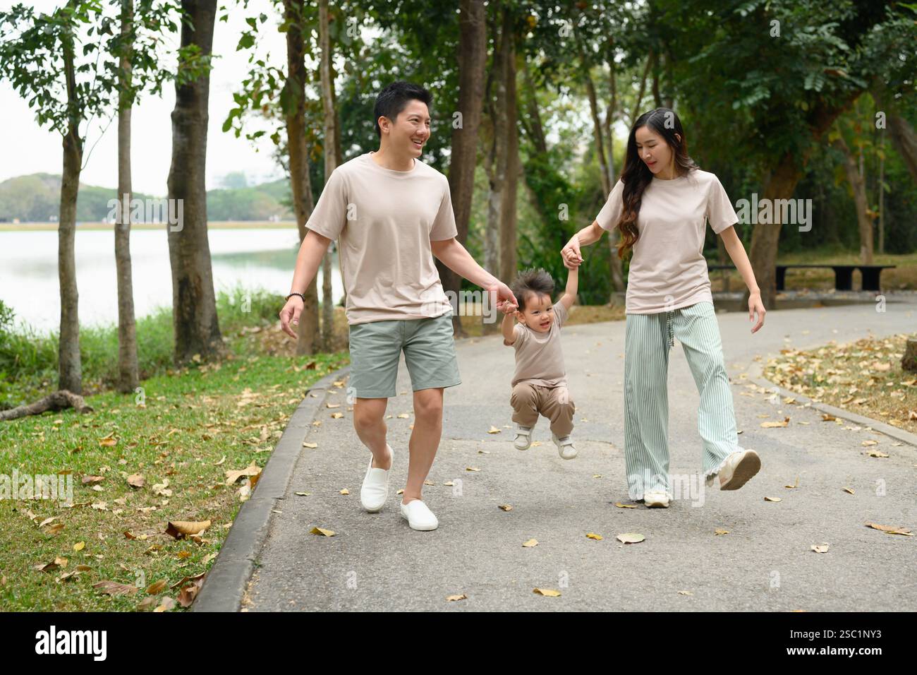 Parents holding their toddler hands while walking along a park path ...
