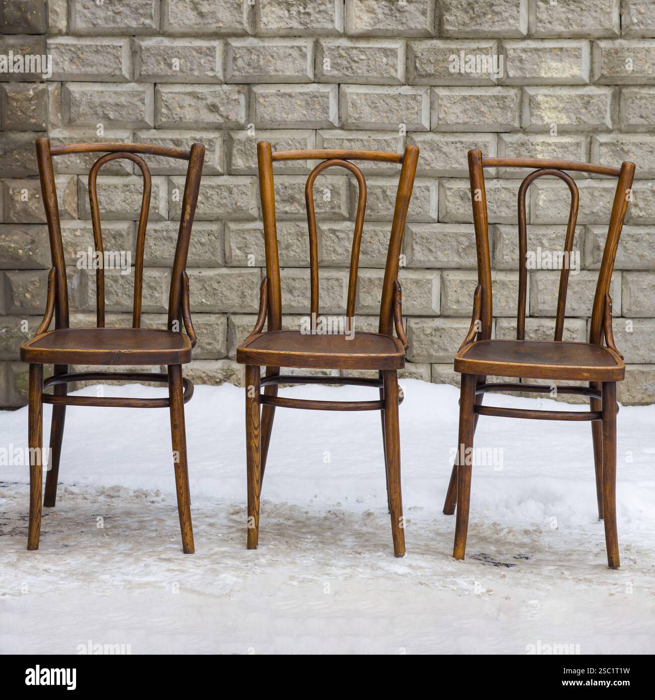 Classic bentwood chairs rest against a brick wall in a snowy landscape ...