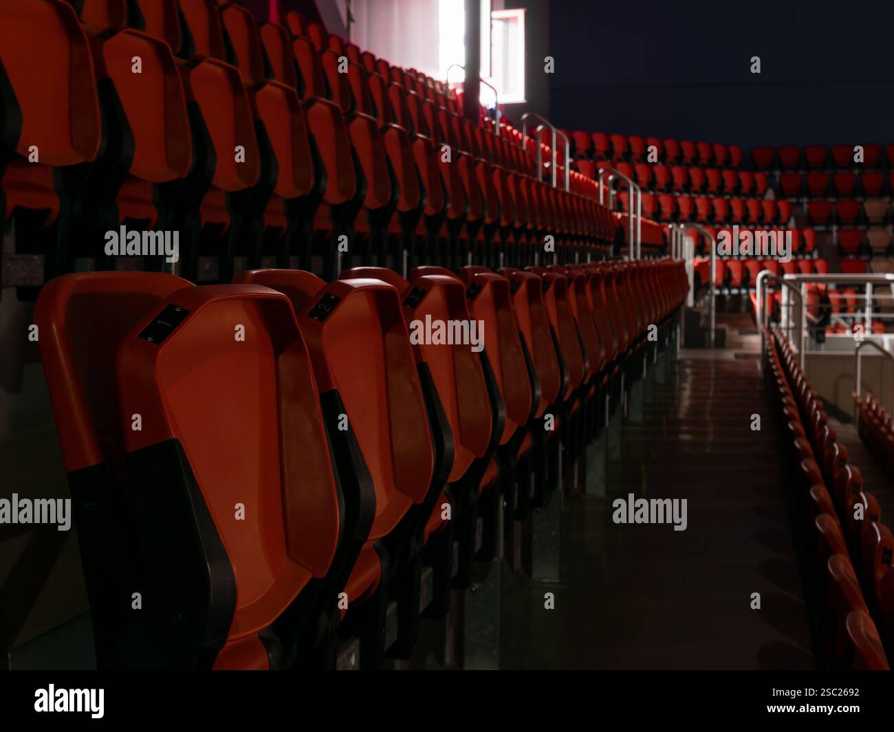 Rows of red seats in the stands of a darkened sports arena illuminated ...