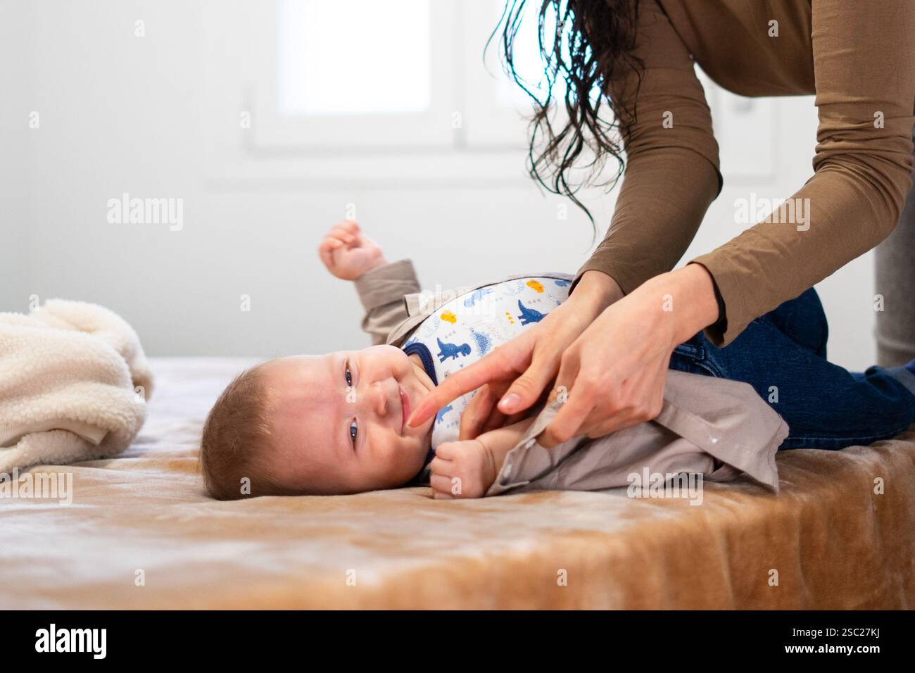 Mother taking care of her baby boy, dressing him on a bed Stock Photo ...