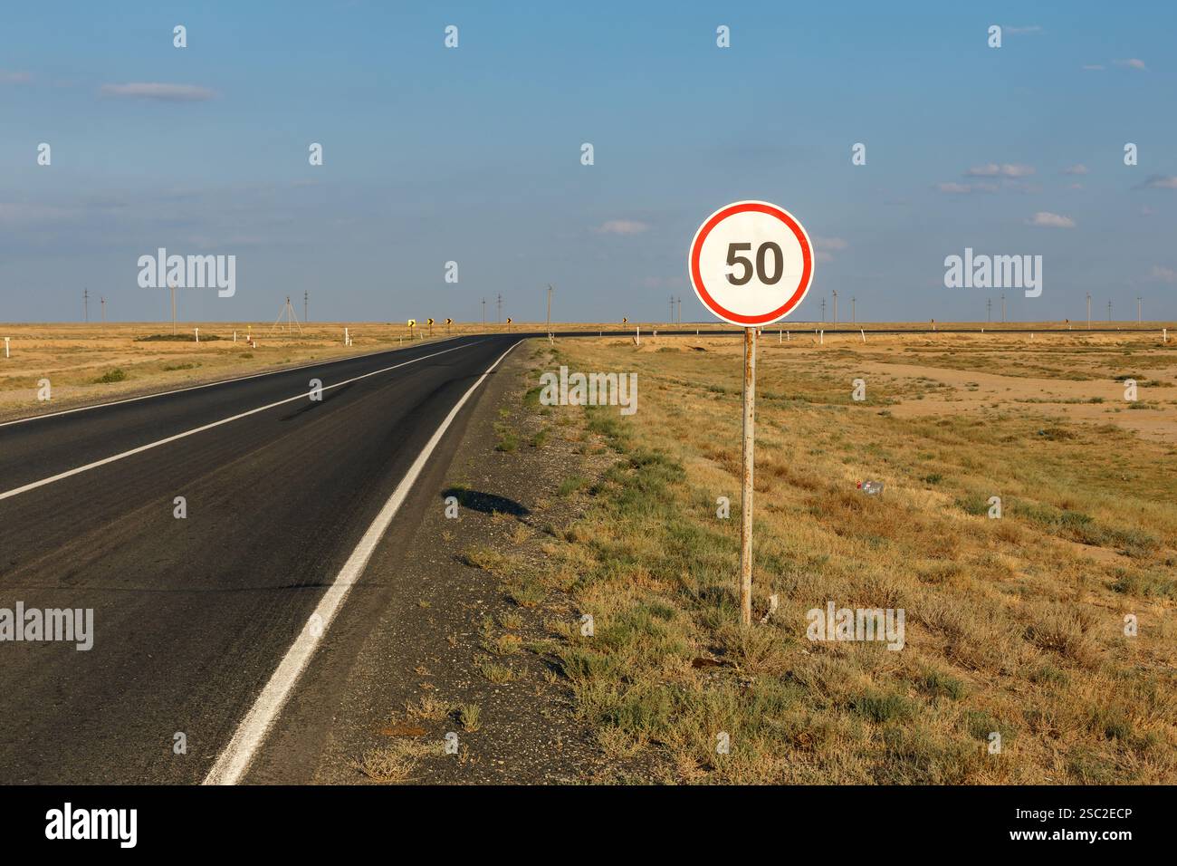 A speed limit sign displays 50 km on a wide road surrounded by arid ...
