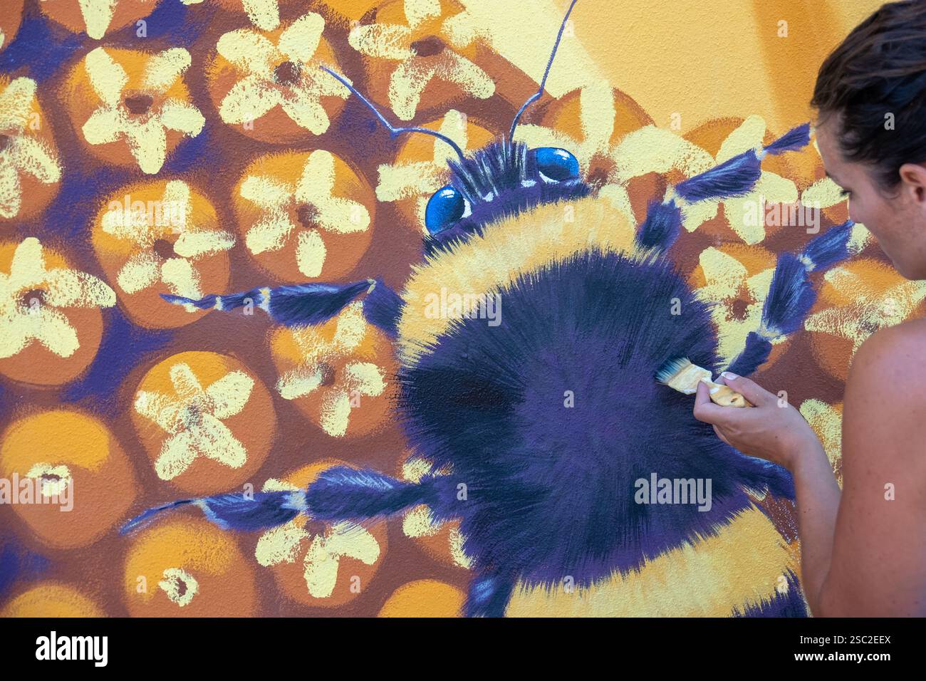female artist paints a vibrant mural of a bumblebee on a honeycomb ...