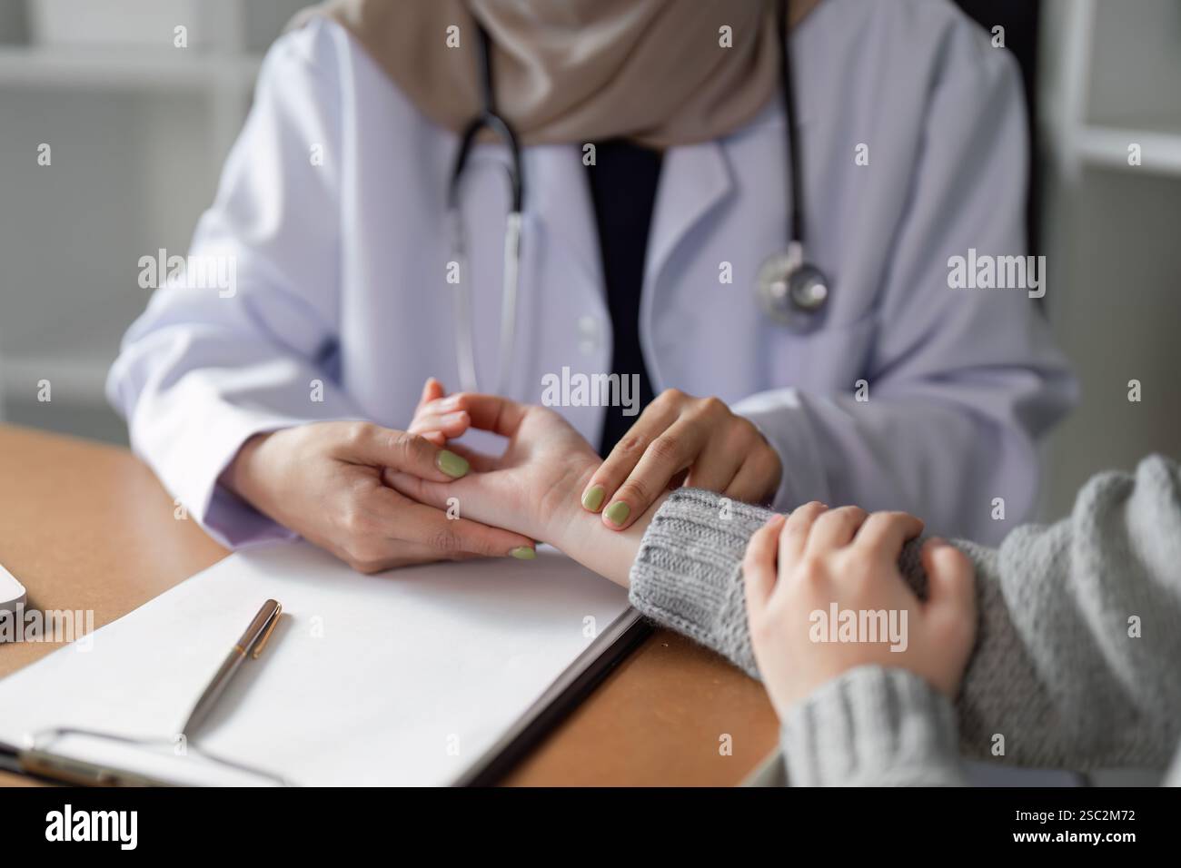 Attentive Muslim female doctor checking a patient's pulse in a modern ...